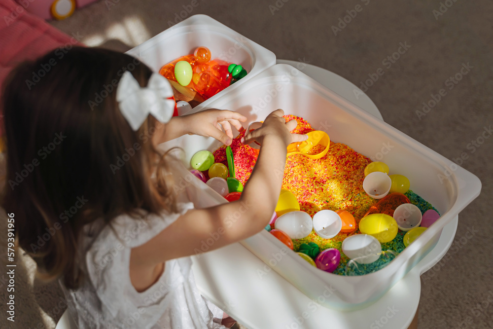 Child playing with colored rice and Easter eggs in sensory bin. Easter ...