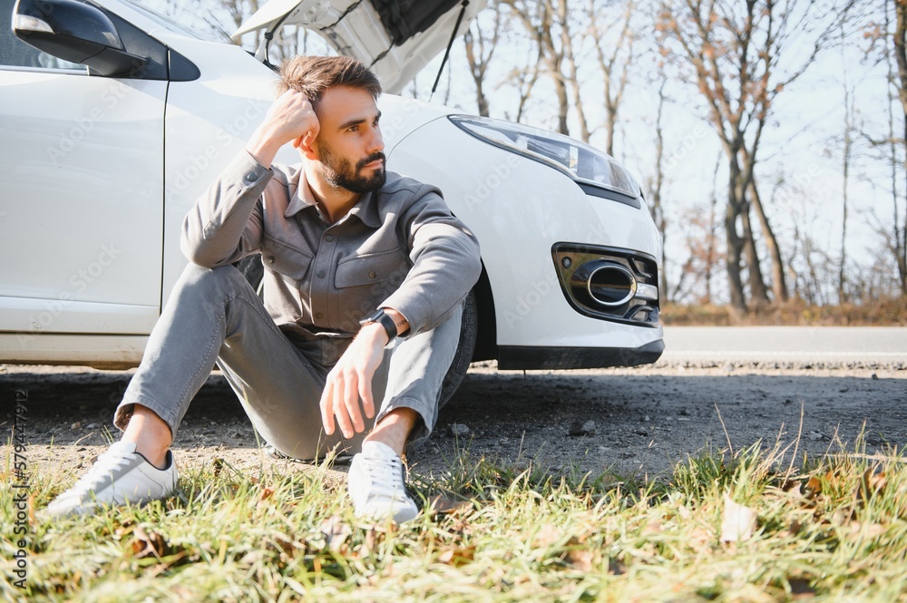 Frustrated sad upset guy driver is sitting near a broken car after road ...