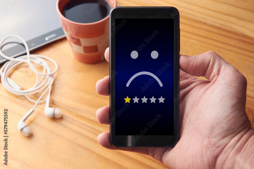 Male hand holding mobile phone with sad face and one star rating. Very ...