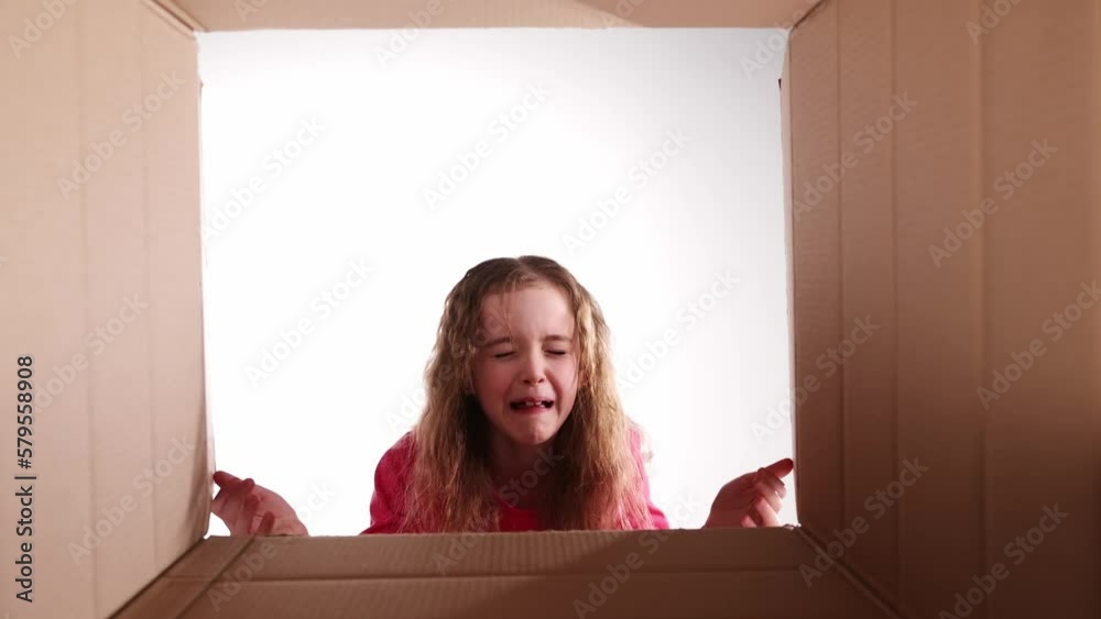 Little girl, child unpacking, opening cardboard box with sad crying ...