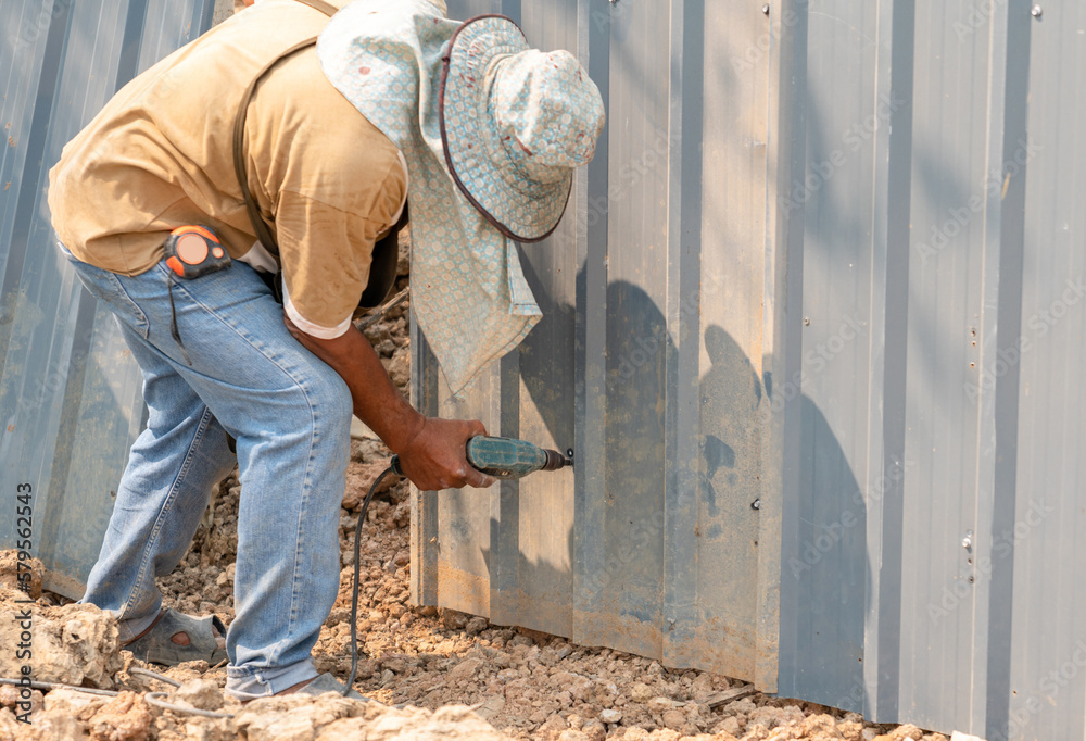 A man's hand in a work to screw screws into a new gray metal sheet ...
