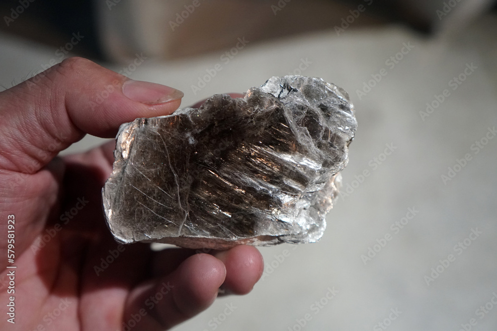 A piece of muscovite mineral isolated on hand. Muscovite is a hydrated ...