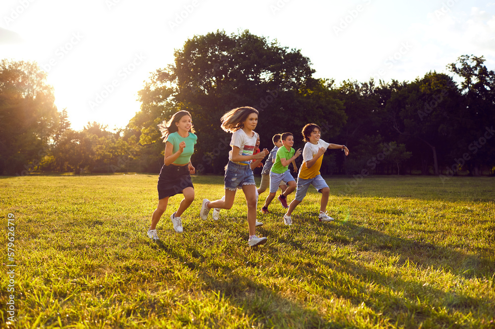 Cheerful carefree teenagers boys and girls run on green lawn competing ...