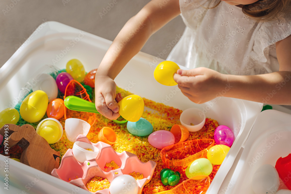 Child playing with colored rice and Easter eggs in sensory bin. Easter ...