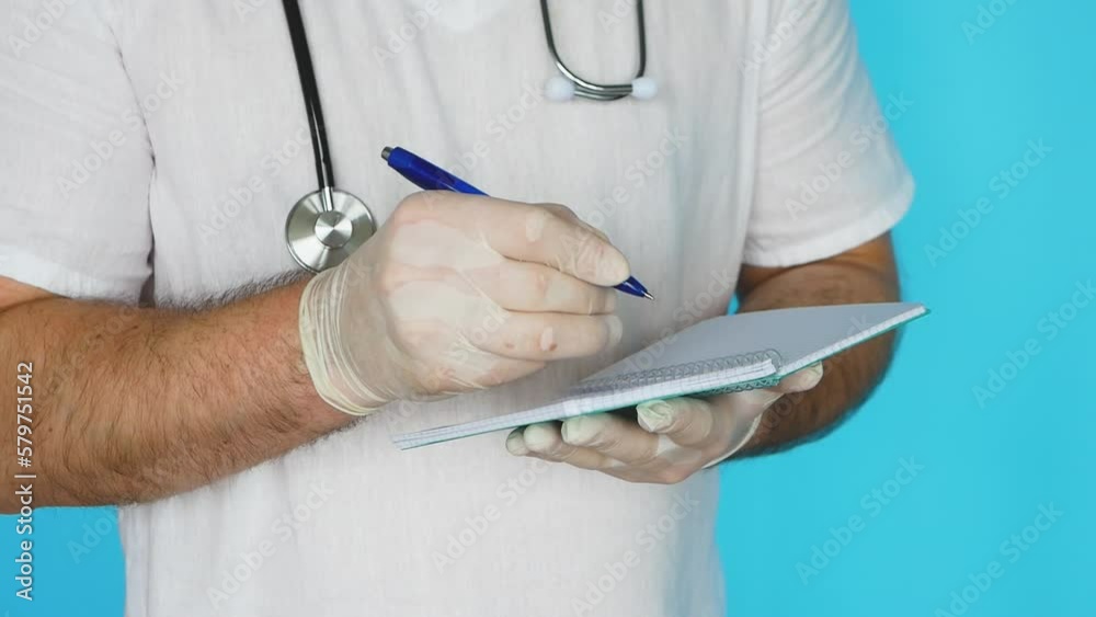A medical worker writes in a journal with a pen on a blue studio ...