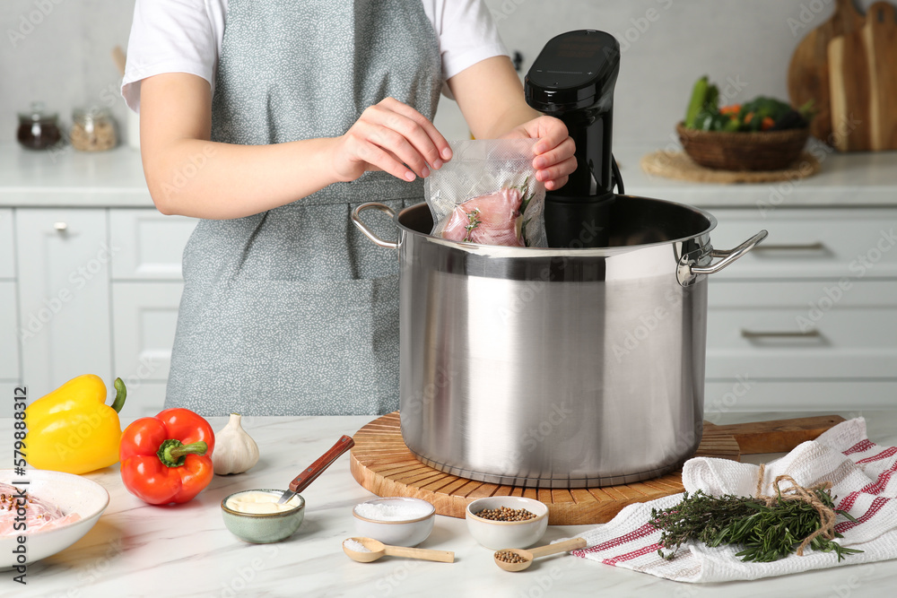 Woman putting vacuum packed meat into pot in kitchen, closeup. Thermal ...