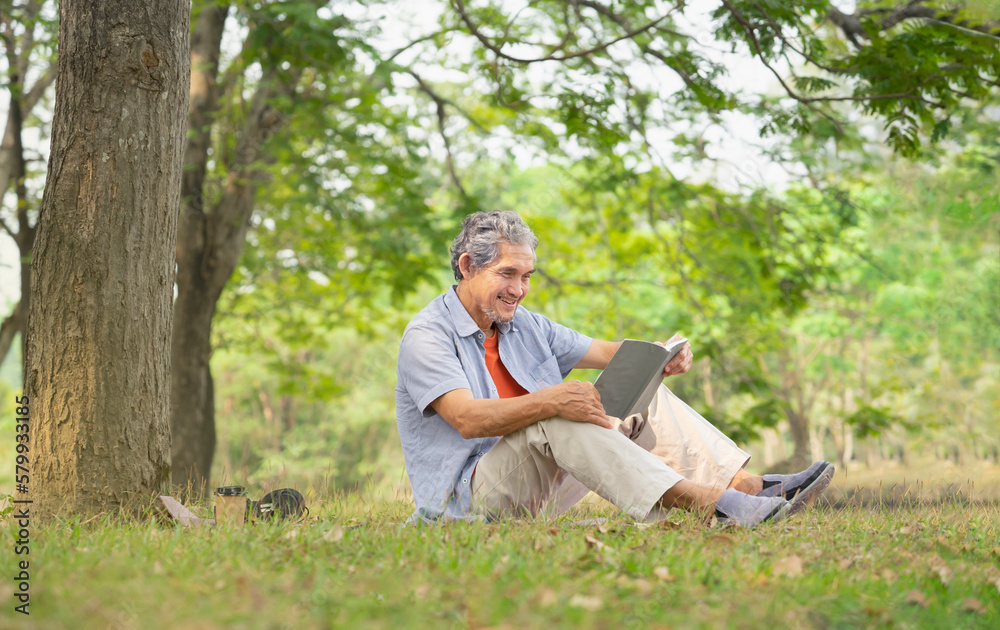 senior man with grey hair holding a book, smiling, sitting near a big ...
