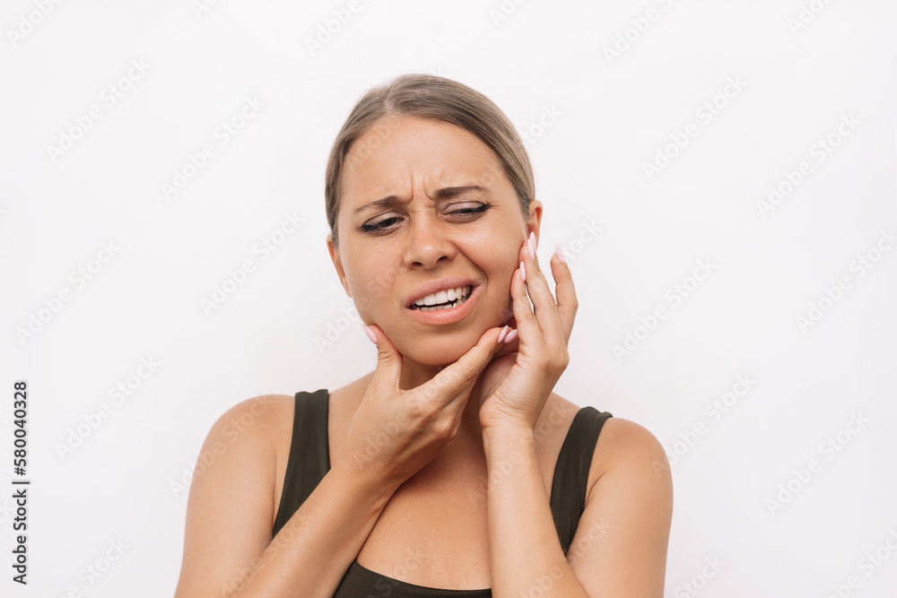 Young caucasian blonde woman suffering from jaw pain holding her chin ...