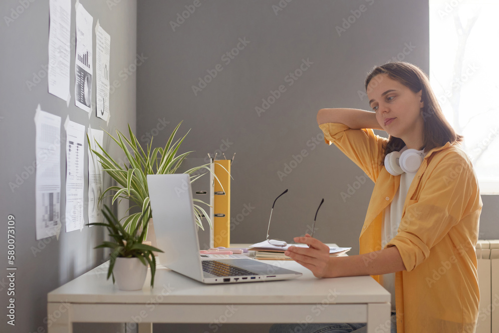 Indoor shot of exhausted woman wearing casual clothing working in ...