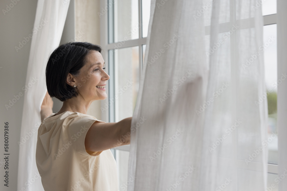 Happy mature homeowner woman looking out of big window, enjoying view ...