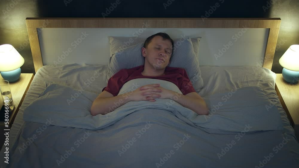 Portrait of a young man falling asleep in his bed at night, arms folded ...