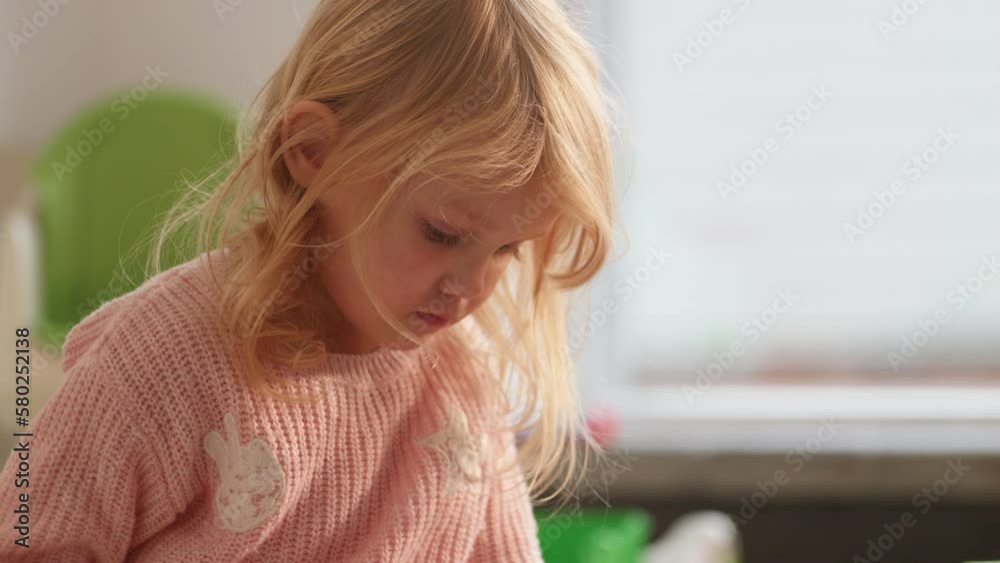 Little cute blond girl plays on the floor busily being alone, autistic ...