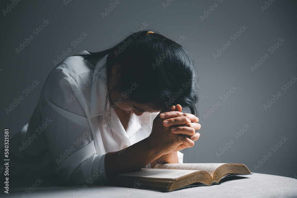 woman kneeling and praying in modern house at sunset time. Female catholic prayer worship to God ...