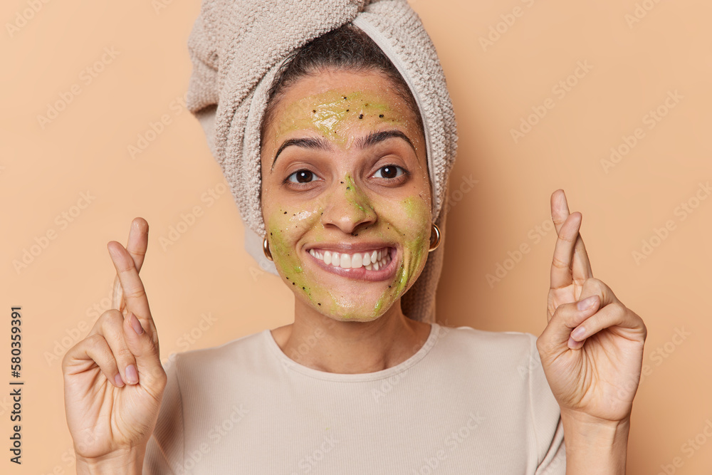 Cheerful hopeful woman bites lips keeps fingers crossed believes in ...