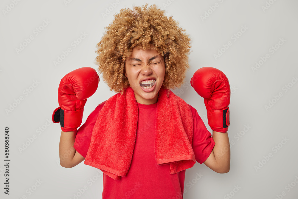 Emotional female boxer with curly hair keeps arms raised wears ...