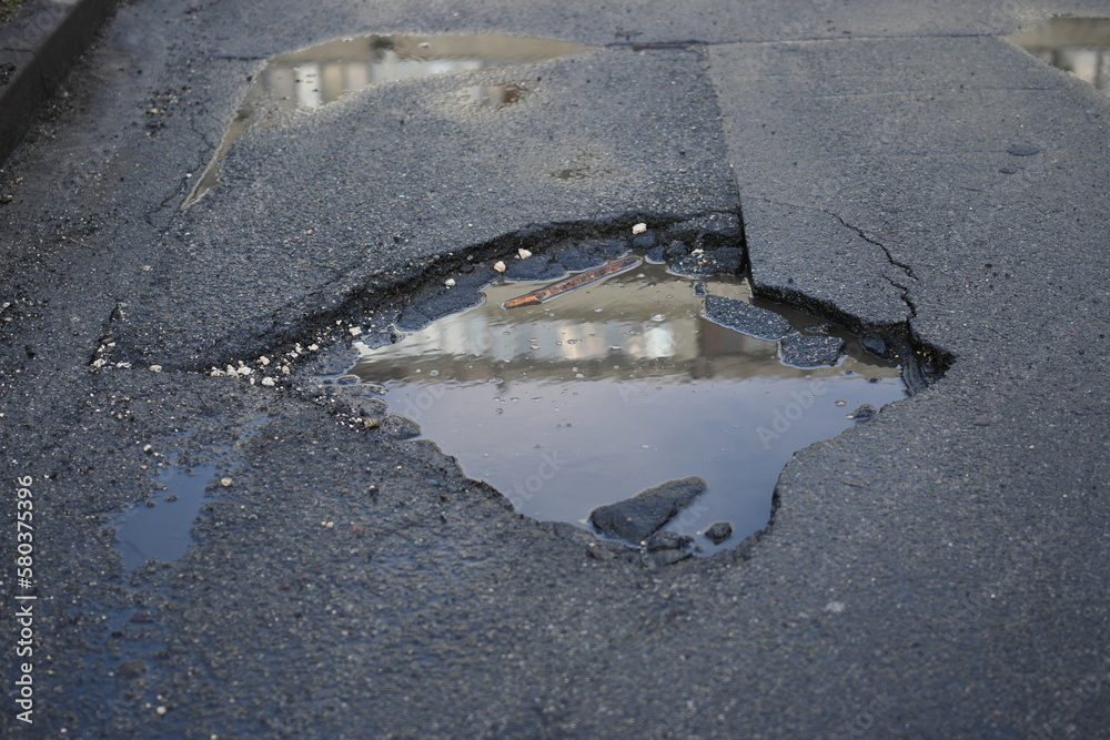 hole in the asphalt, a puddle with muddy water, a destroyed road, the ...