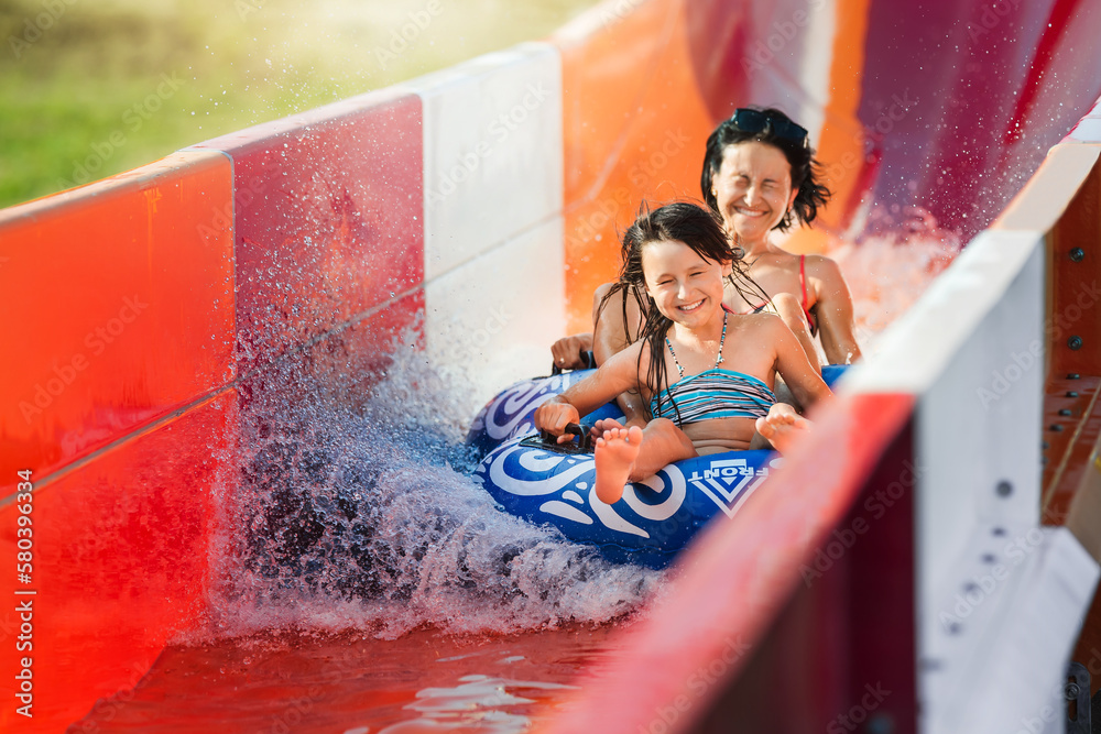 Mother And Daughter Sliding Down Water Slide Sitting Together At