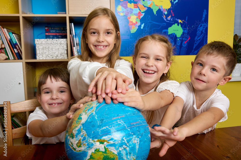 Cheerful children, with joyful smile, put hands together on globe in ...