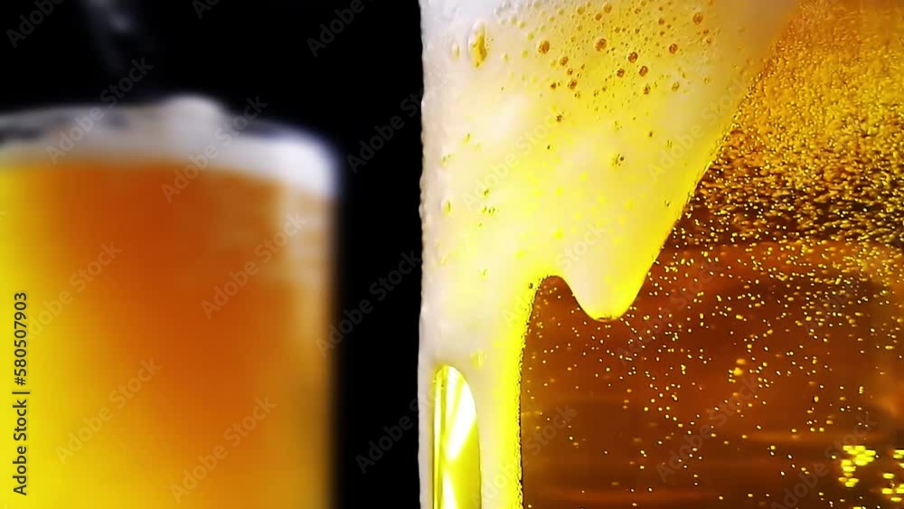 Beer is pouring into a two beer mugs with bubbles close-up on a black ...