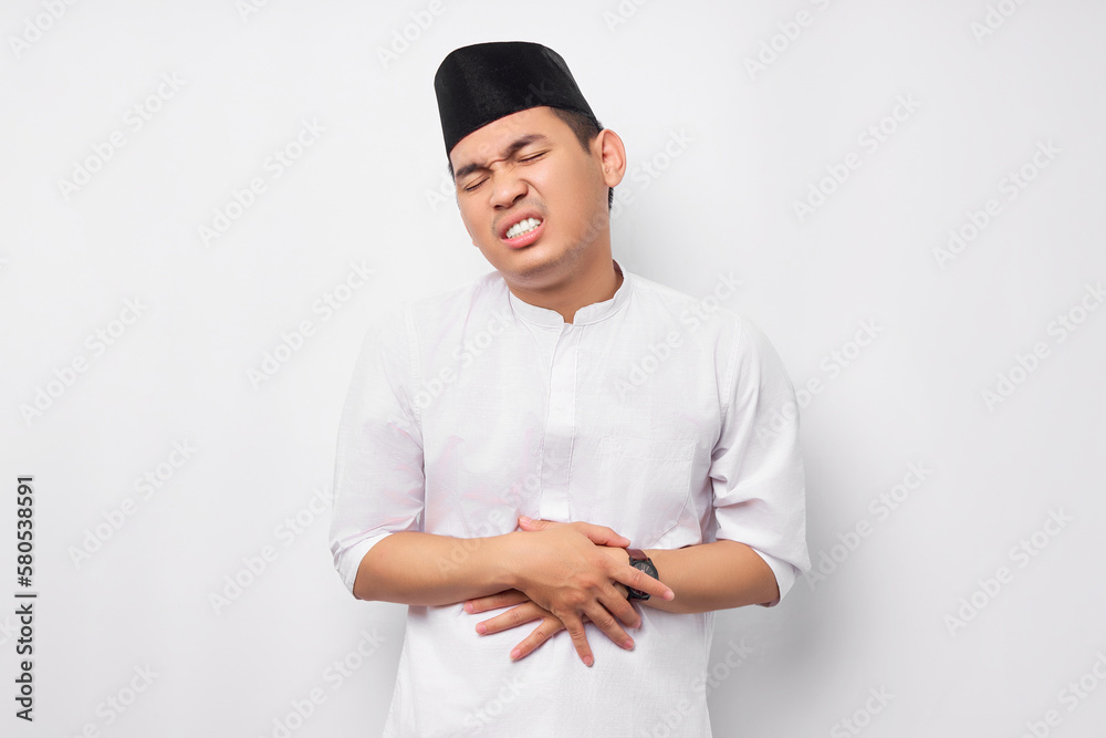 Portrait of sick young Asian Muslim man touching a hand on his stomach ...