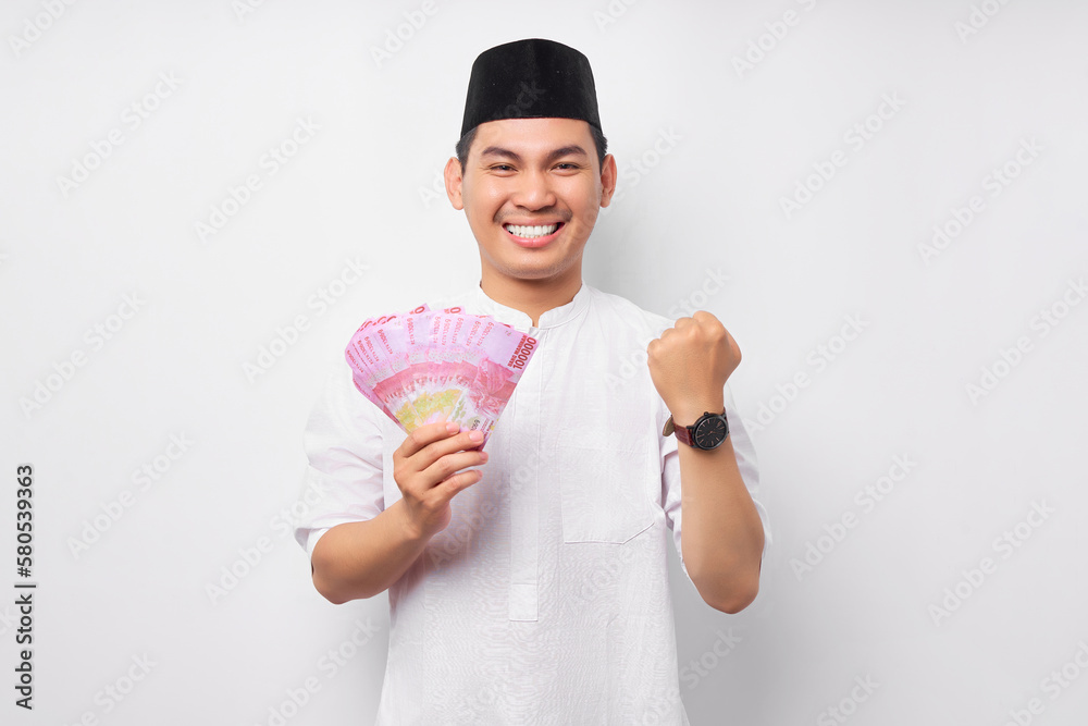 Excited young Asian Muslim man holding cash money rupiah banknotes and ...