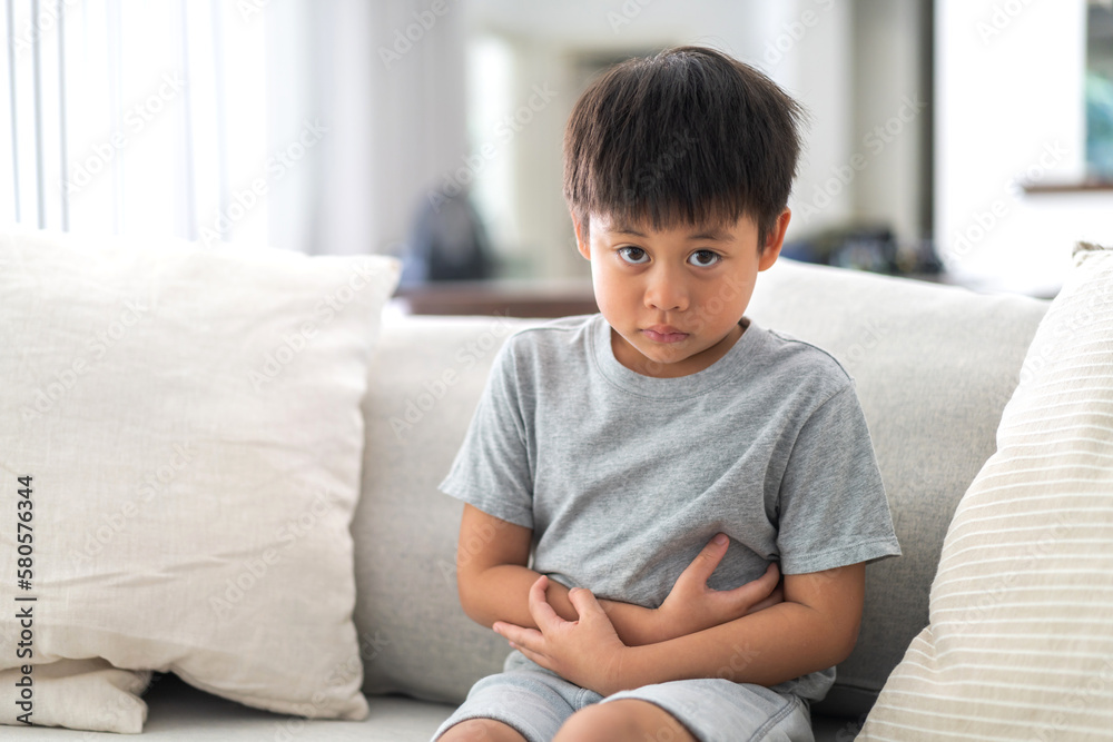 Portrait of sick unhappy little child asian boy touching belly stomach ...