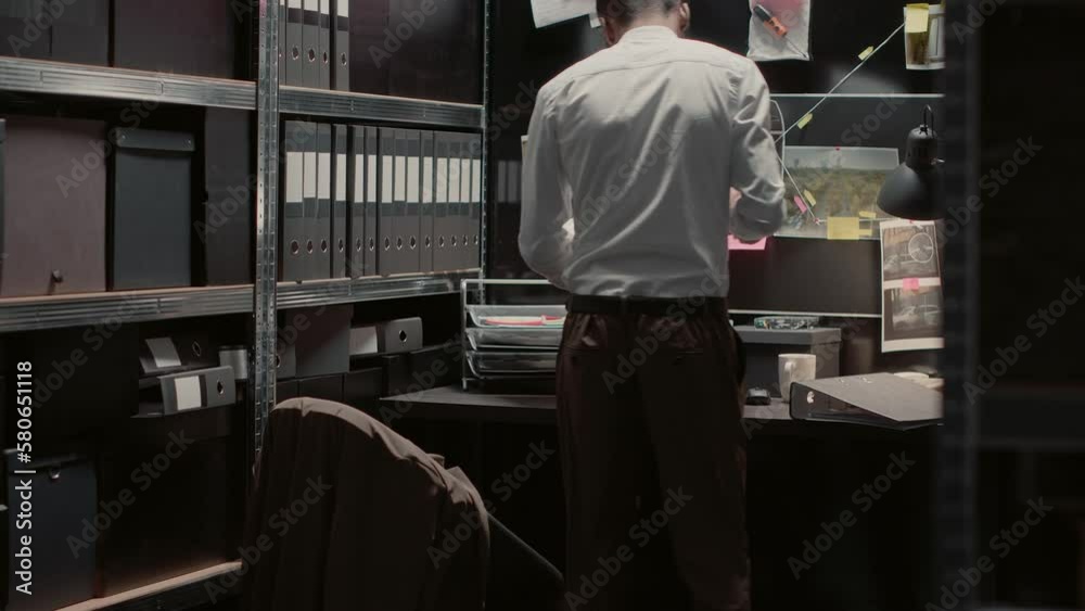 Detective sitting at desk analyzing evidence map on wall, examining law ...
