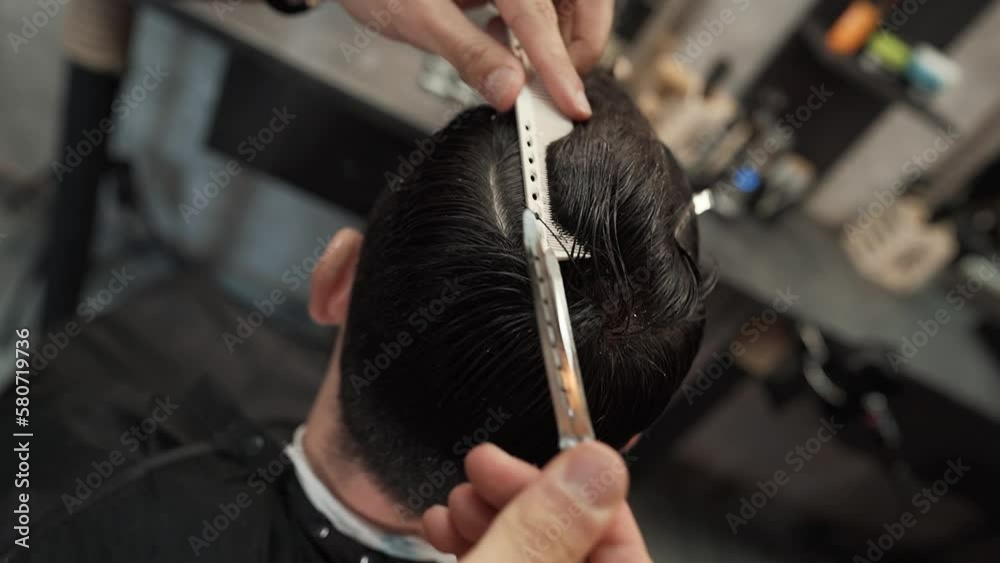 Close -ups of trendy barber cuts bearded man's hair with a scissors in ...