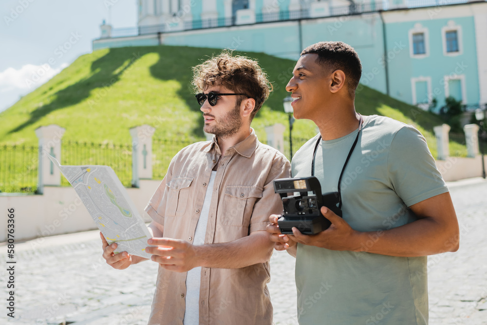 tour guide in sunglasses looking at map near african american traveler ...