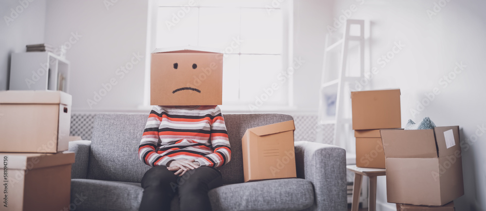 Tired sad woman with cardboard box on her head sitting on the sofa in ...
