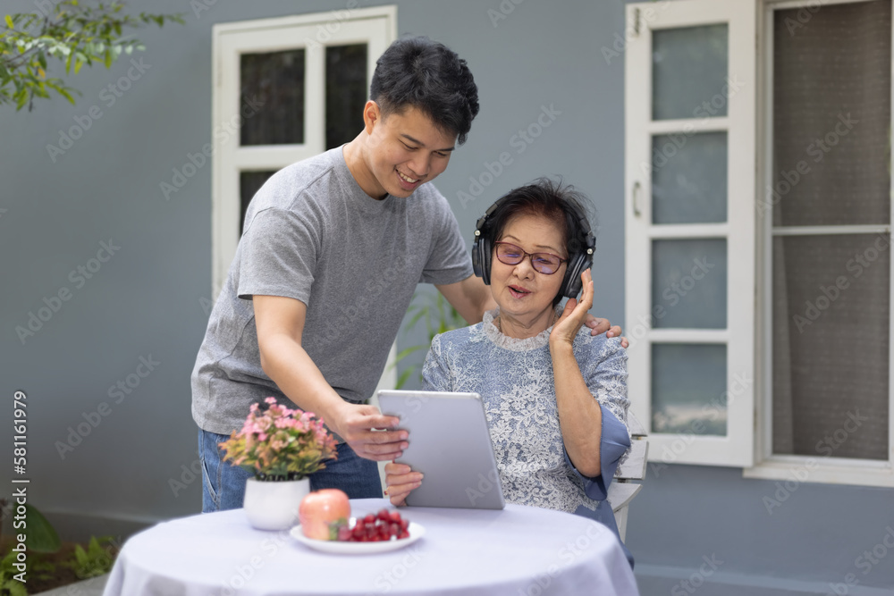 Grandson helping grandmother using computer tablet for listen music and ...