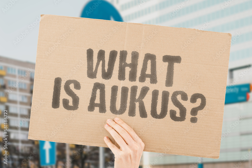 The question " What is AUKUS? " is drawn on a carton banner in men's ...