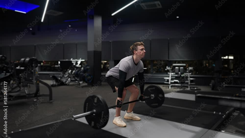 Fitness man trains in a modern gym and does an exercise with a barbell ...