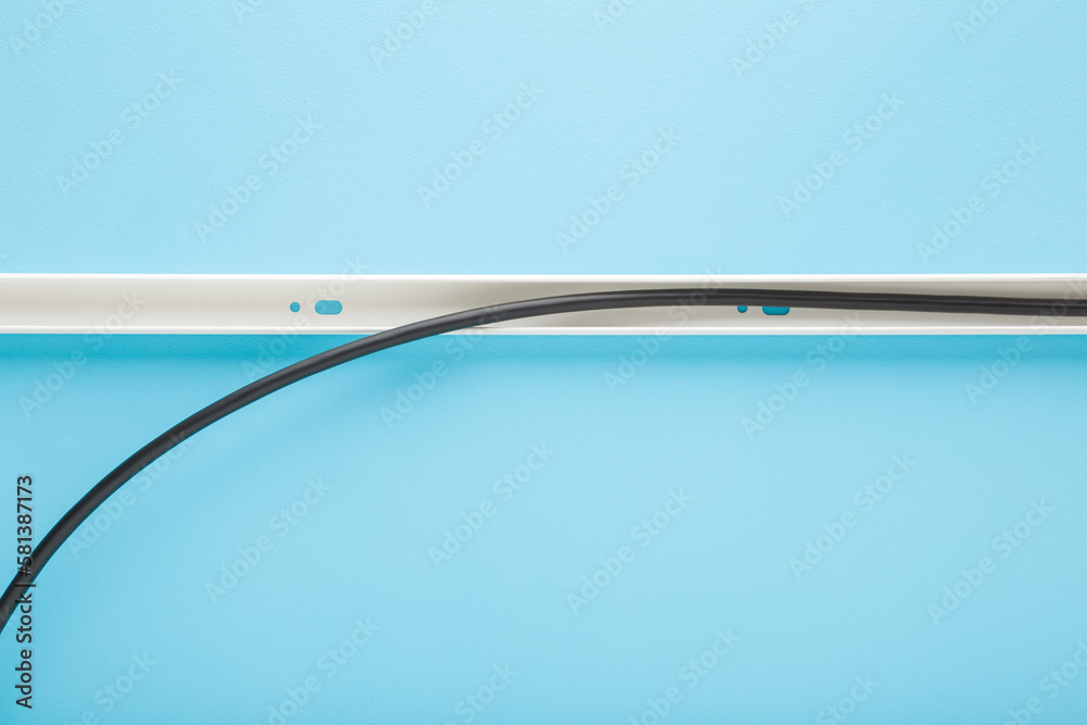 Dark black new wire in white plastic channel on light blue table ...