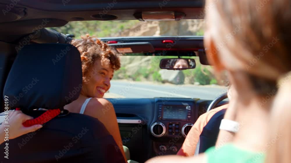 Group of female friends in open top car laughing on road trip through ...