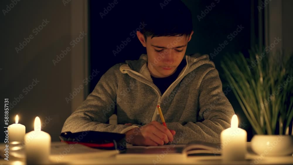 Poor young rural boy from informal settlement writing and learning lessons by candlelight ...