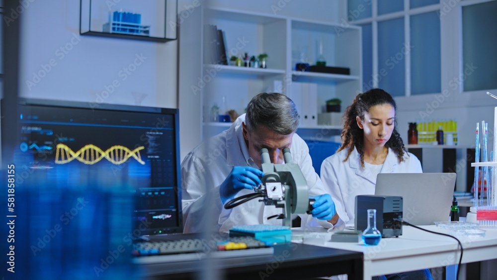 Lab researchers examining biological material under microscope, drug ...