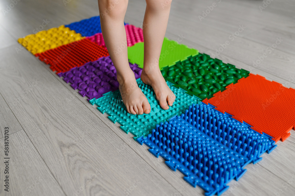 The child walks on an orthopedic massage mat for legs of different ...