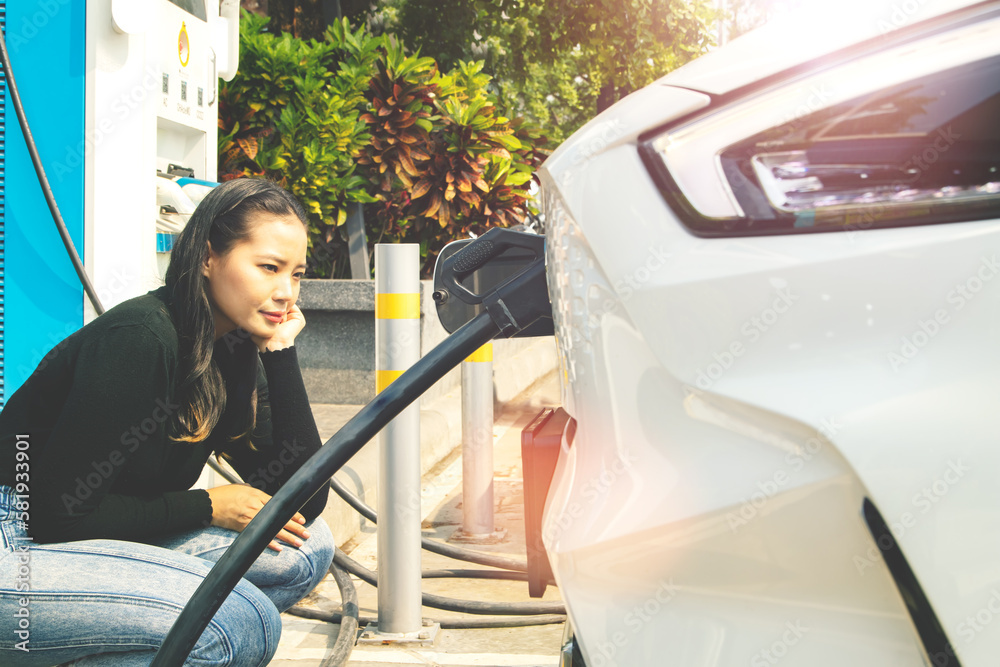 Young asian woman driving modern white EV electric vehicle sitting in ...