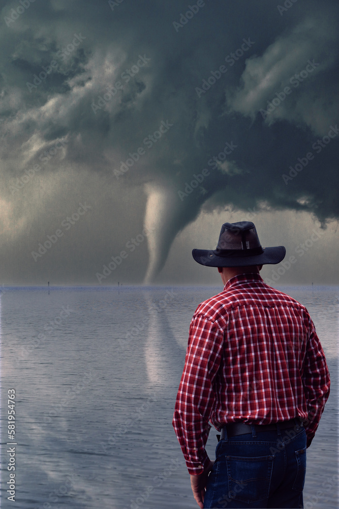 Man wearing a black hat watching a tornado over a lake. Storm chaser ...