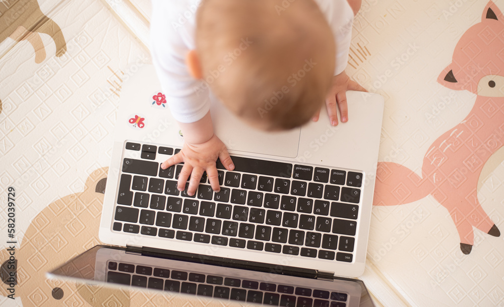 Baby's hands is typing on laptop. Hebrew and English keyboard. Top view ...