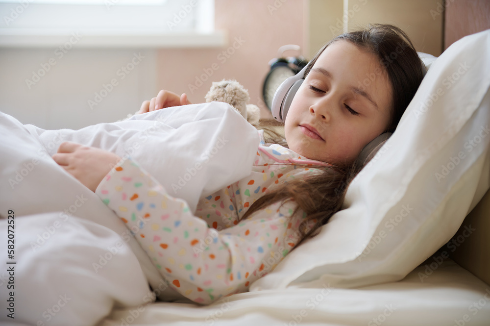 Adorable child girl in headphones, napping in a white bedroom, falling ...