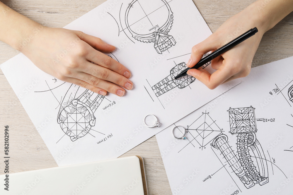 Jeweler drawing sketch of elegant ring on paper at wooden table, top ...