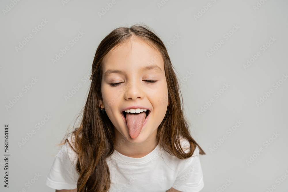 Preteen kid sticking out tongue and closing eyes isolated on grey ...