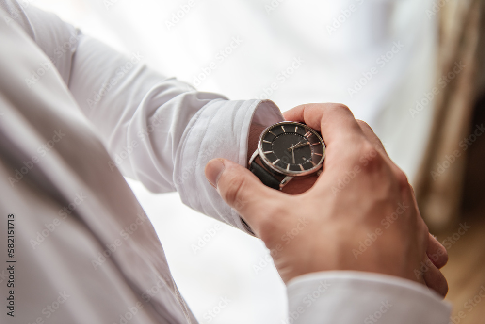 A man in a white shirt puts an expensive watch on his hand and holds ...