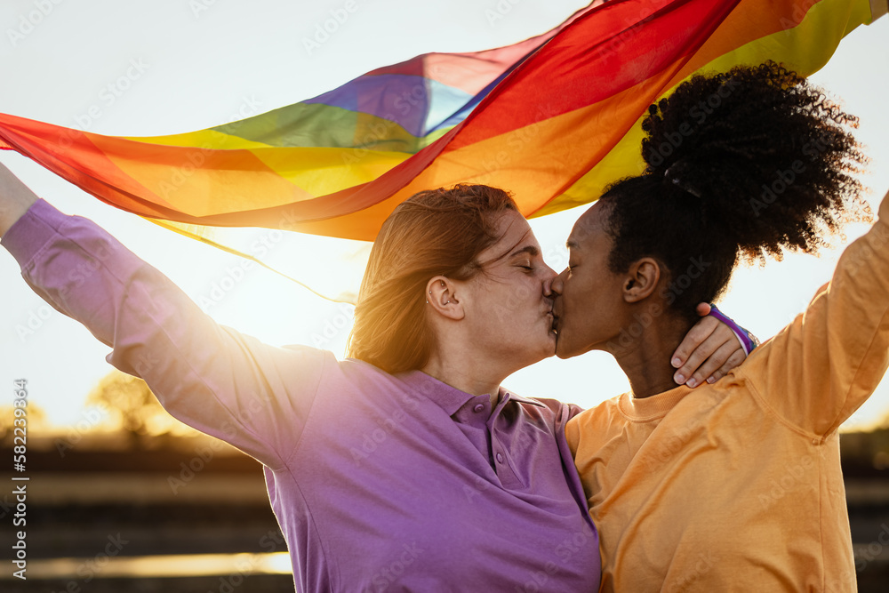 Foto de Lesbian couple kissing while holding rainbow flag during gay pride celebration outdoor ...