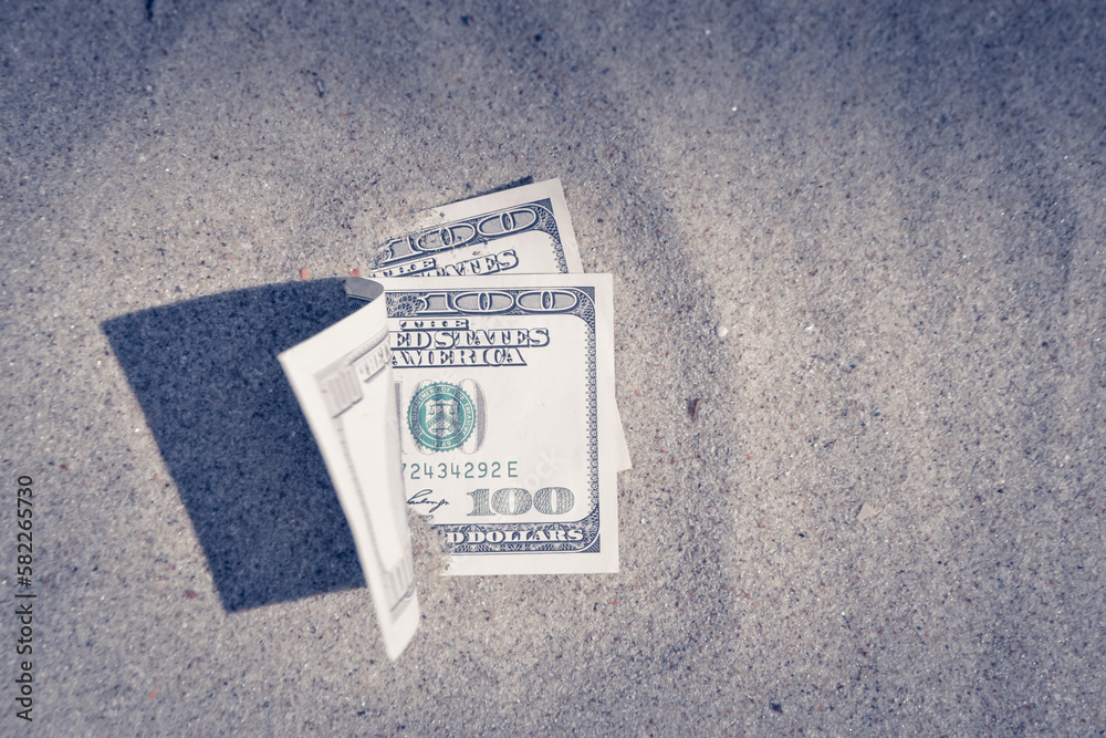 Foto de Money dollars half covered with sand lie on beach close-up ...