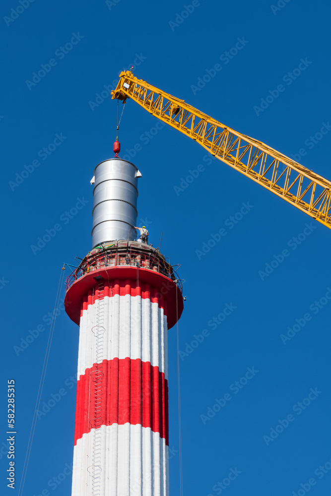 Top of tall factory chimney at renovation with crane arm on blue sky ...