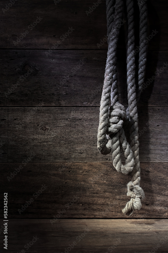 An old, frayed, grey, length of rope hanging down on a rustic wooden ...