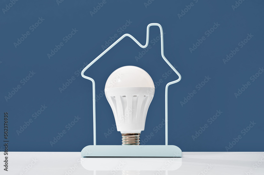 Glowing LED light bulb inside house frame on blue background. Green ...